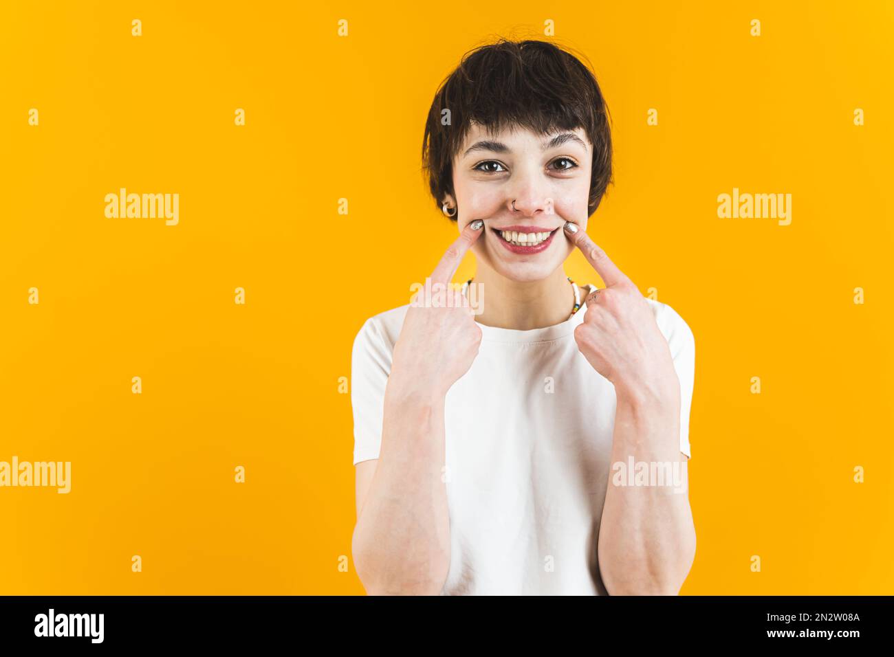 Adorable positive young adult girl looking at camera and touching her ...