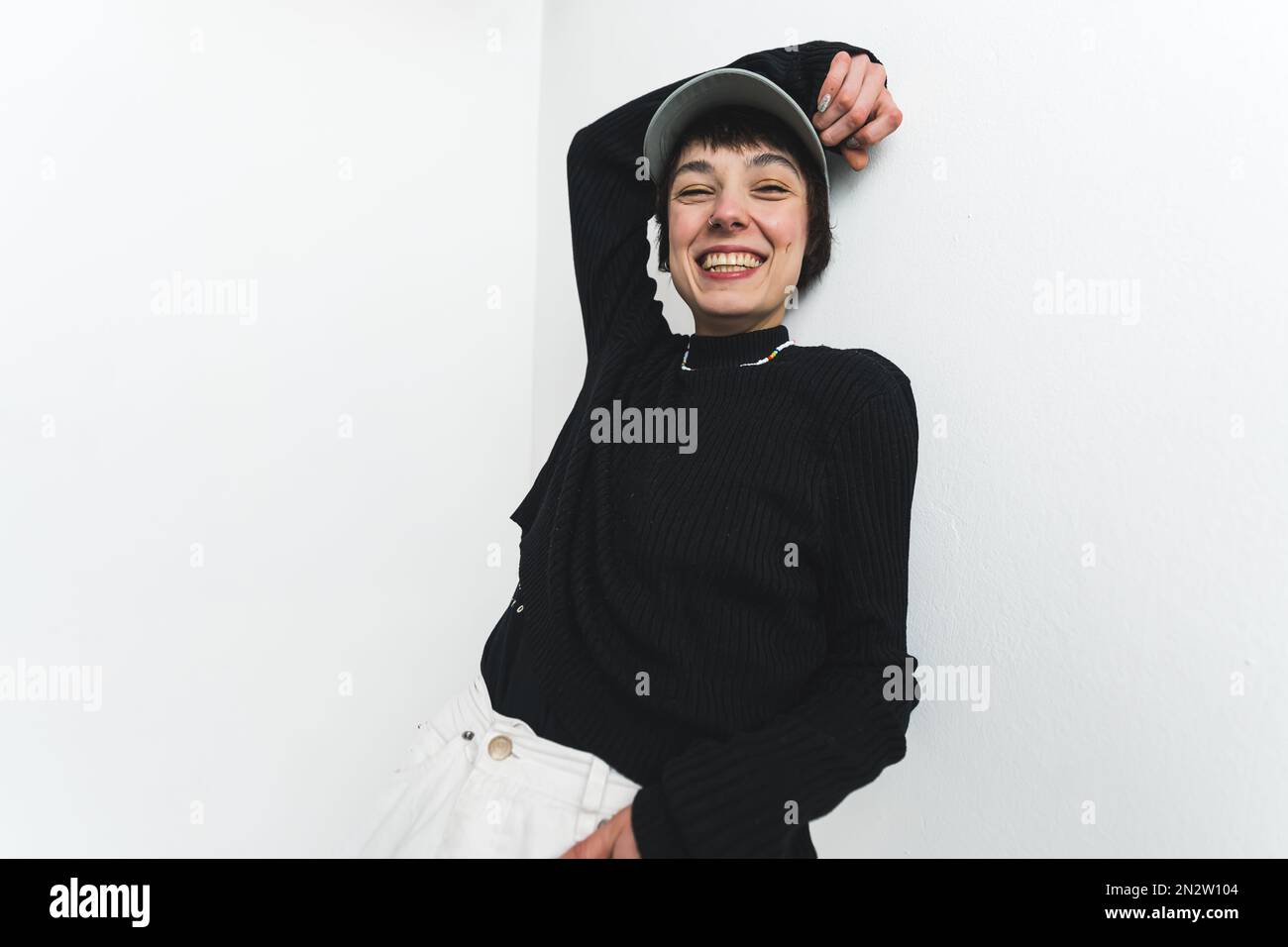 Youthful boyish-looking woman in black turtleneck and gray cap laughing ...