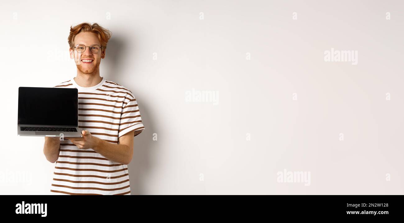 Smiling proud redhead guy showing empty laptop screen. Handsome young ...