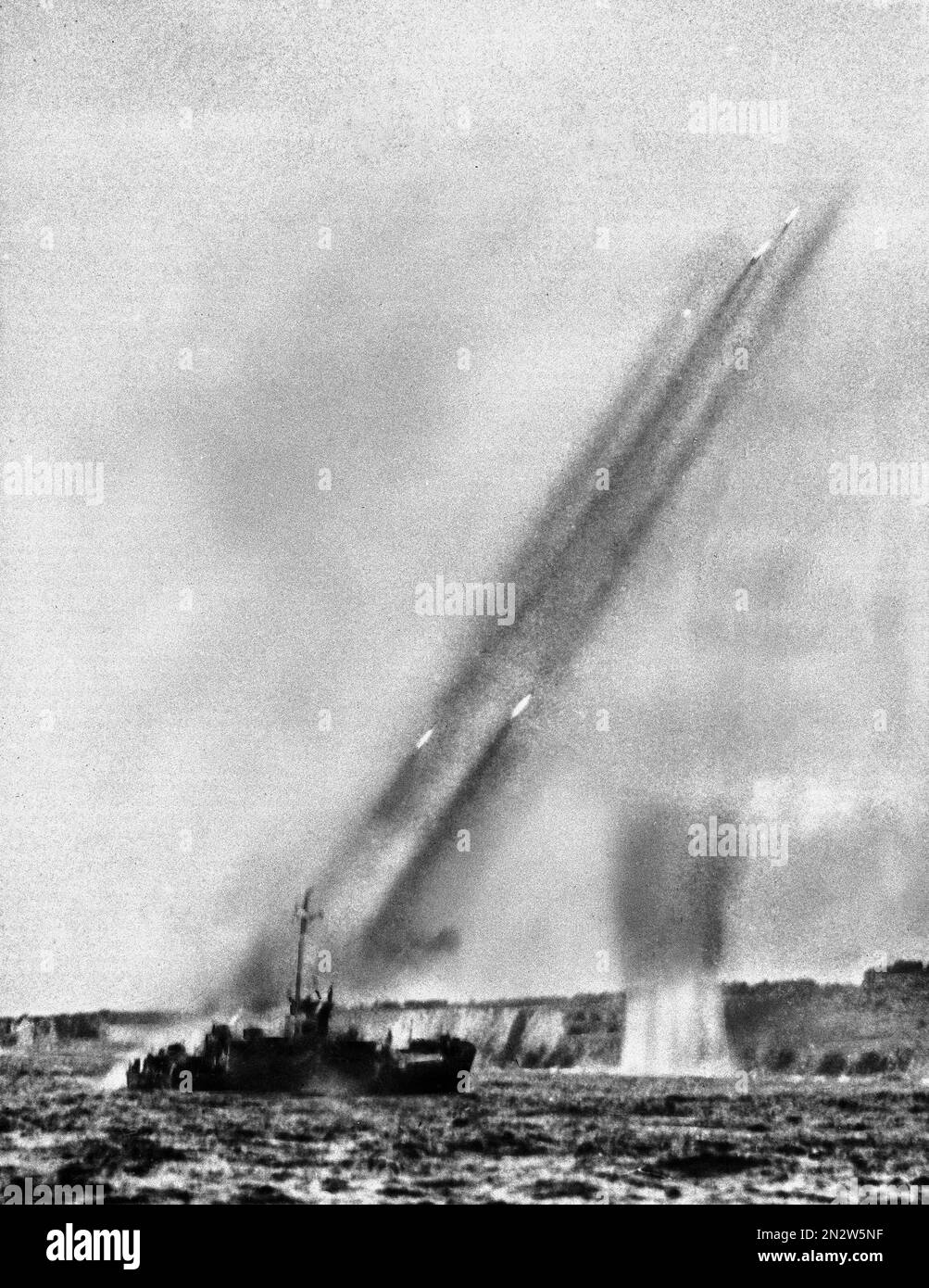 A U.S. landing craft fires rocket projectiles at the rugged shore of ...