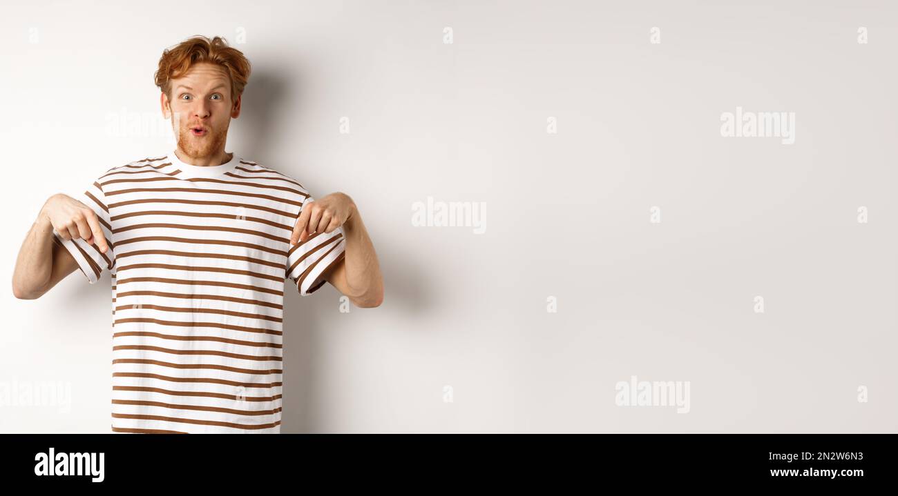 Image of funny redhead male student pointing fingers down, showing ...