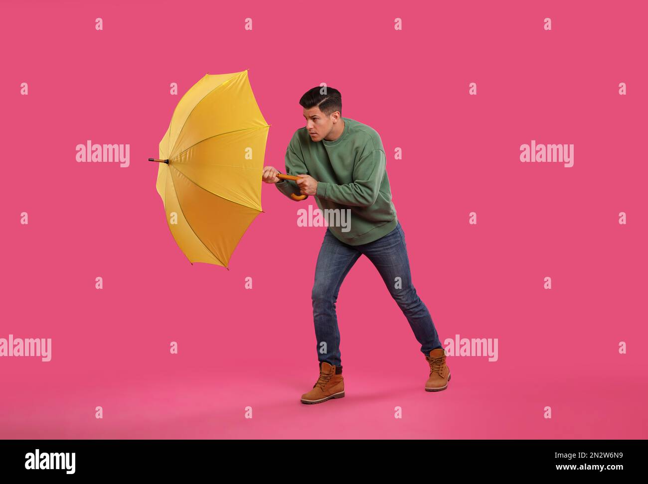 Emotional man with umbrella caught in gust of wind on pink background ...