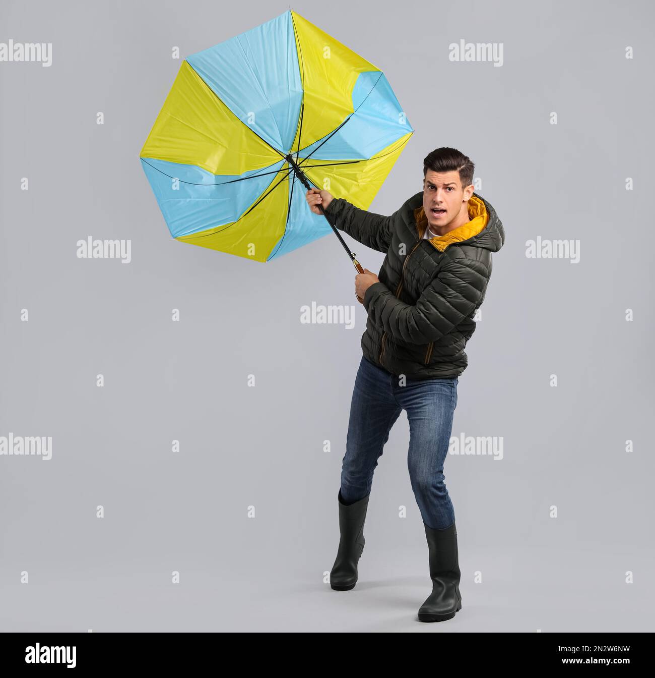 Emotional man with umbrella caught in gust of wind on grey background ...
