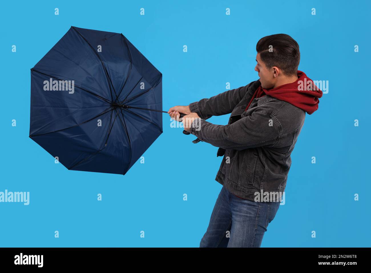 Man with umbrella caught in gust of wind on light blue background Stock ...
