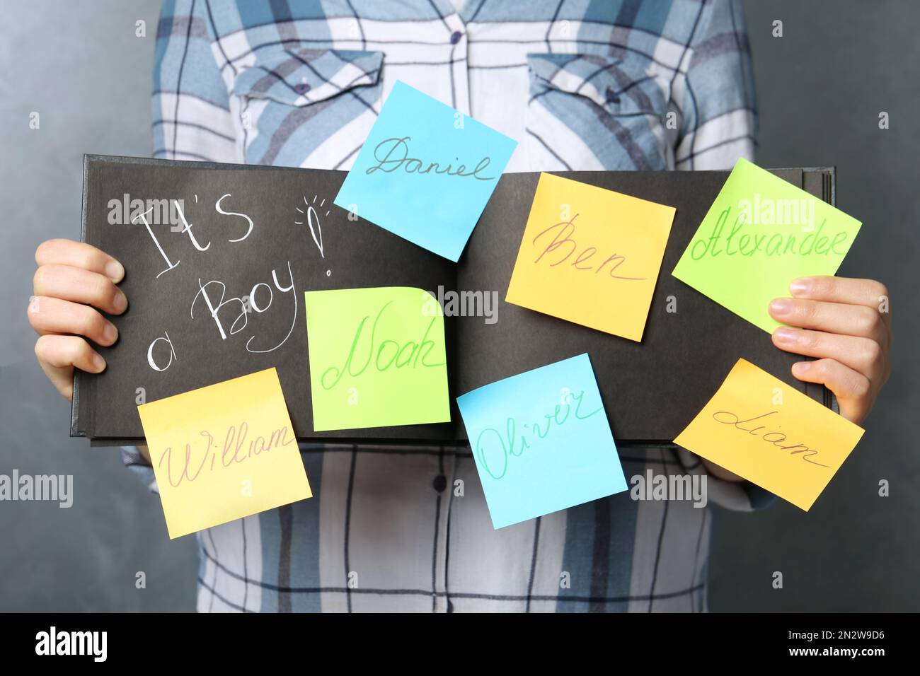 Woman holding notebook with written different baby names on grey ...