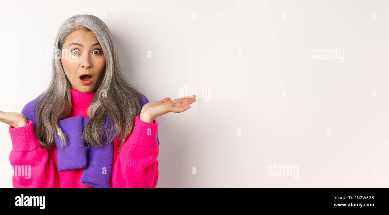 Close up of shocked asian mom staring at camera, spread hands sideways ...