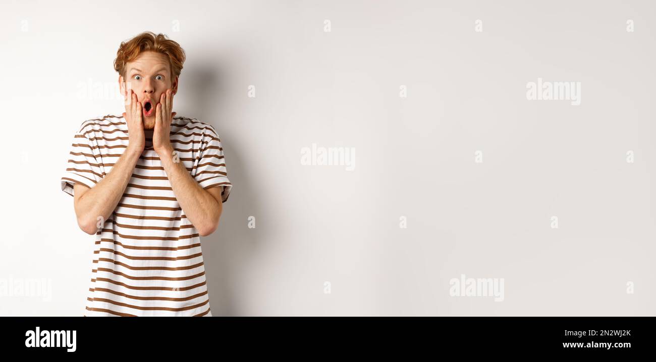 Impressed young man with ginger hair, gasping and staring shocked at ...