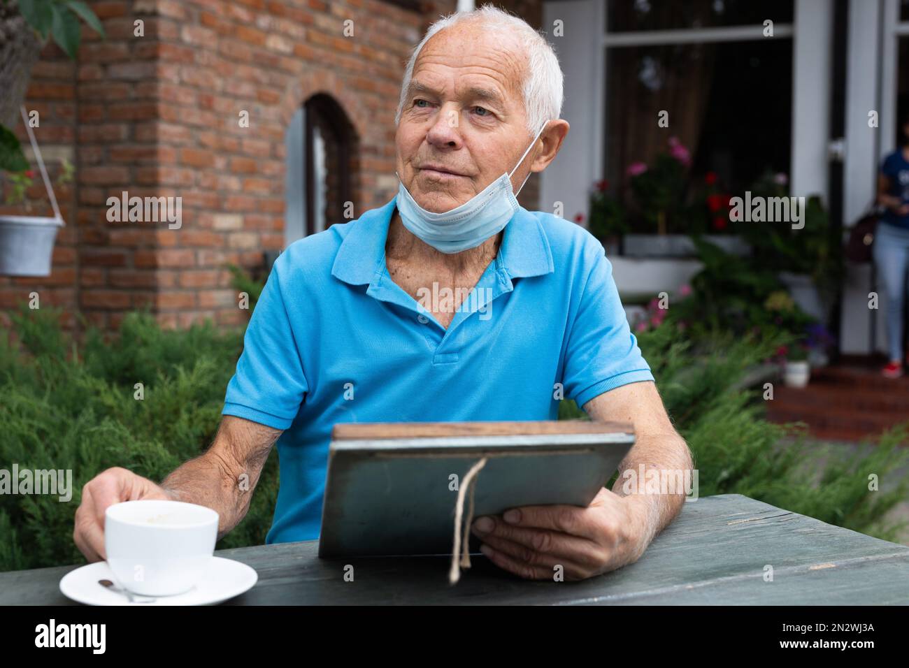 Senior man in protective mask chooses dish from the menu while sitting ...