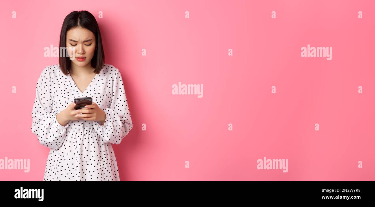 Nervous and concerned asian woman reading message on smartphone ...