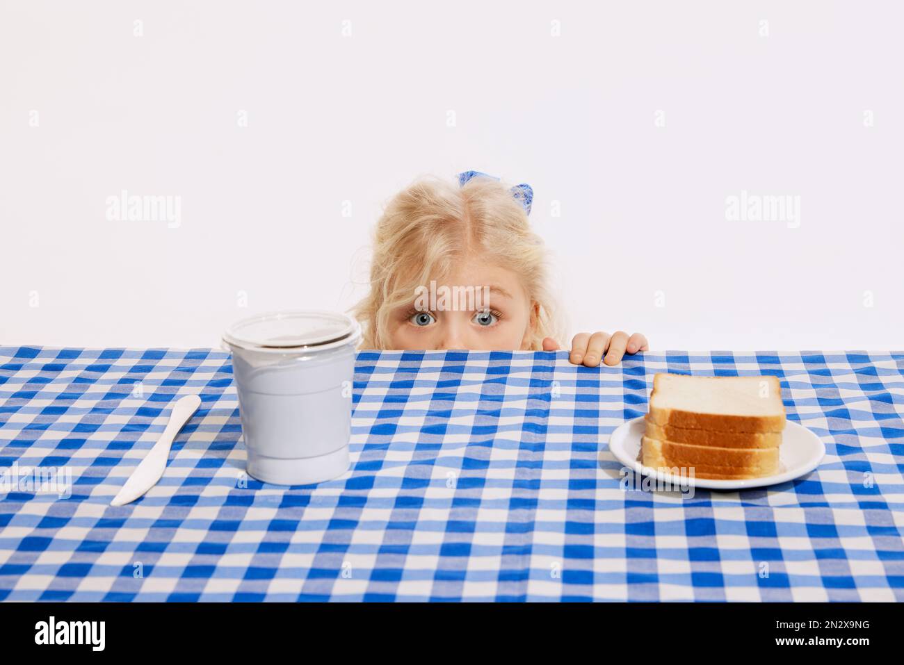 Little cute girl looks out from behind table with fear in her eyes ...