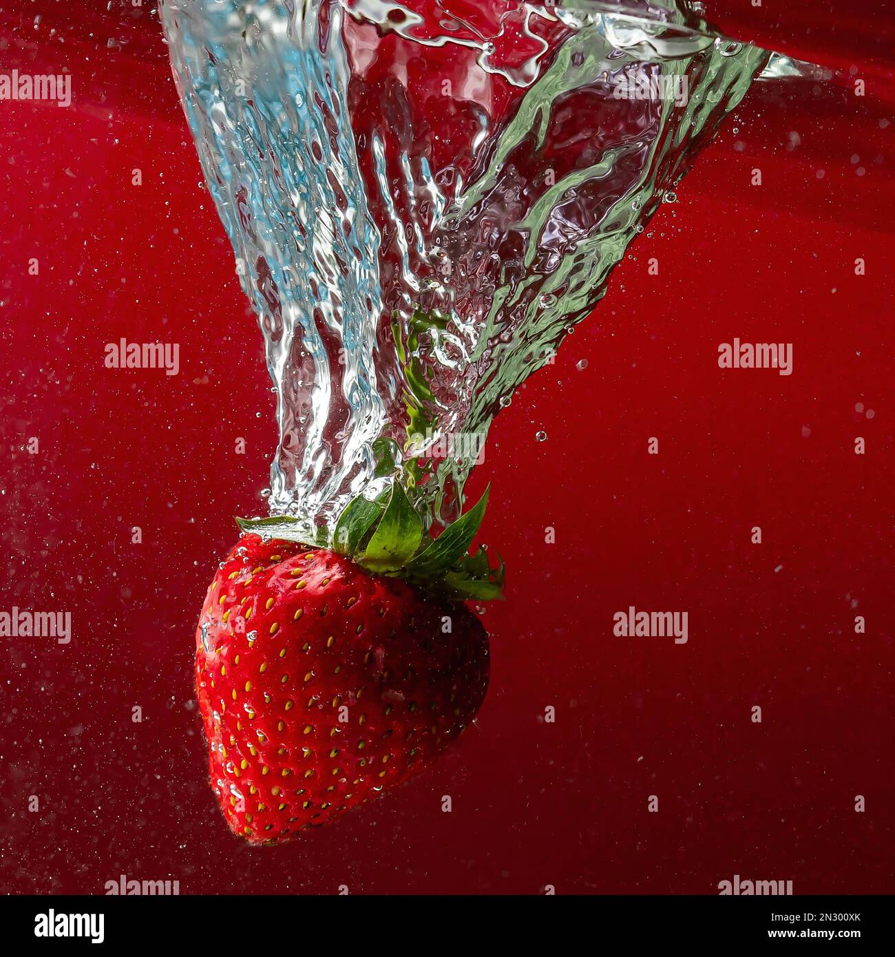 ripe strawberries fall into the water lifting splashes and air bubbles ...