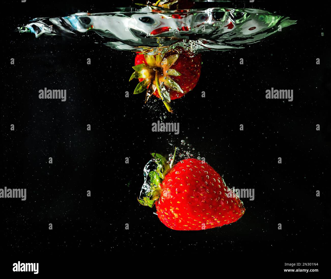 ripe strawberries fall into the water lifting splashes and air bubbles ...