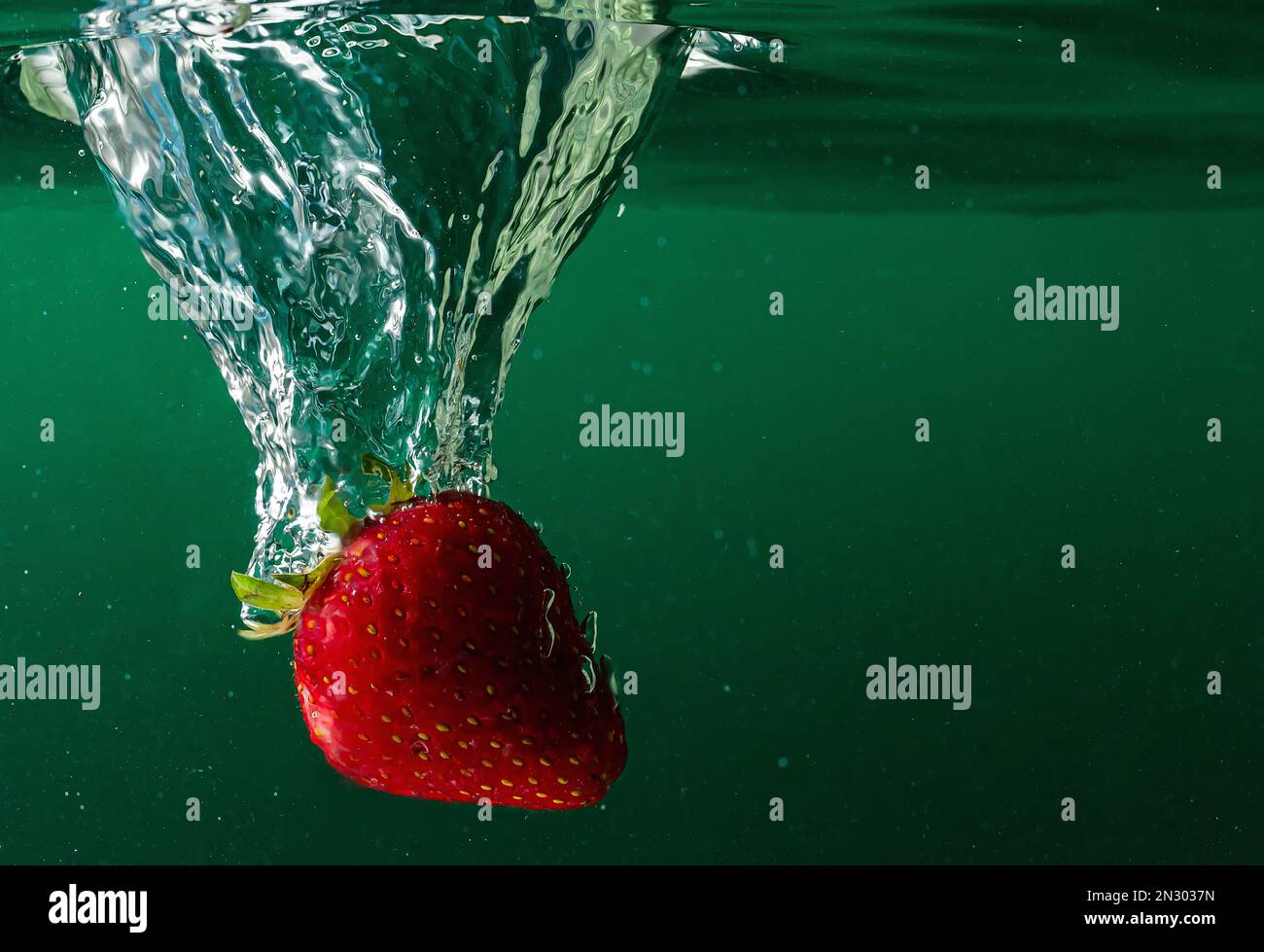 ripe strawberries fall into the water lifting splashes and air bubbles ...