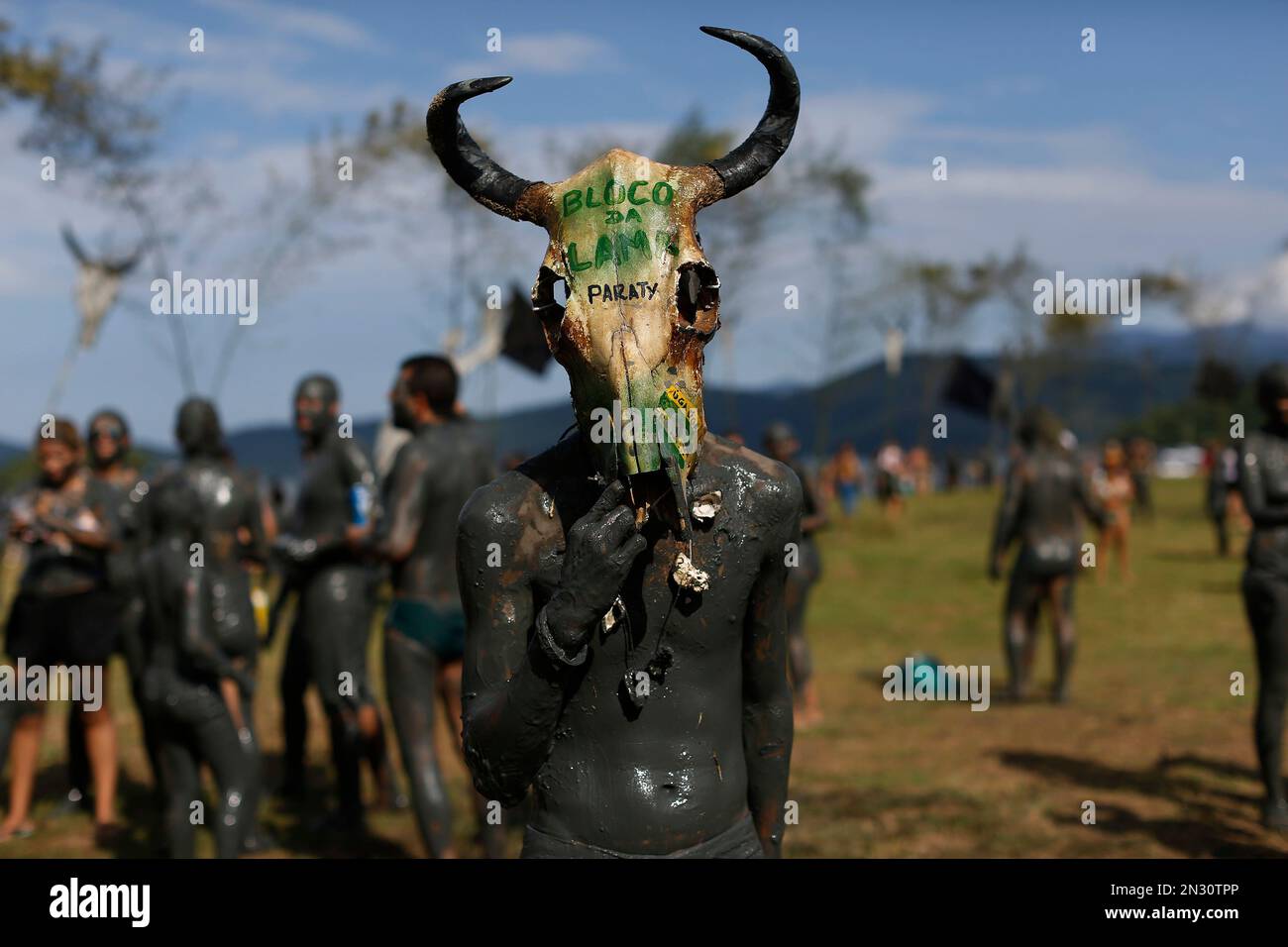 A mud covered reveler wearing a cow's skull as a mask poses for a photo ...