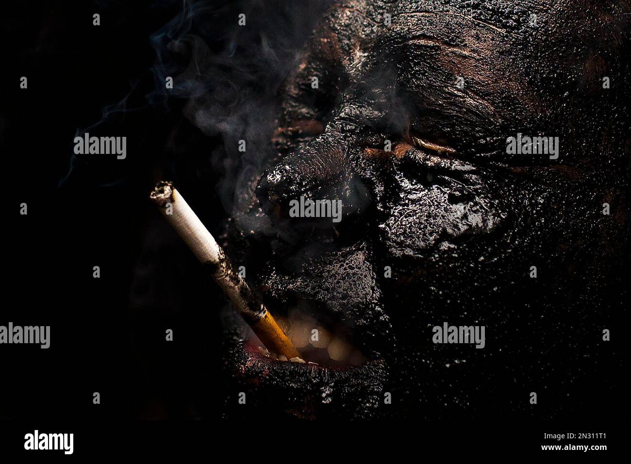 A man, covered in oil and soot representing the devil, smokes a ...