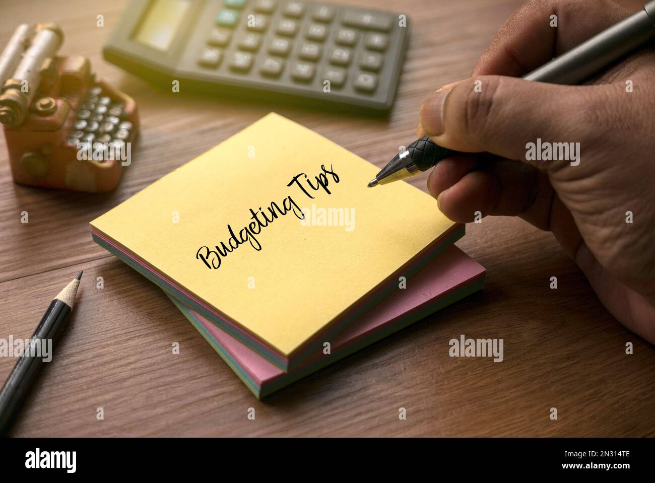 A hand writing Budgeting Tips on a yellow memo note with calculator and ...