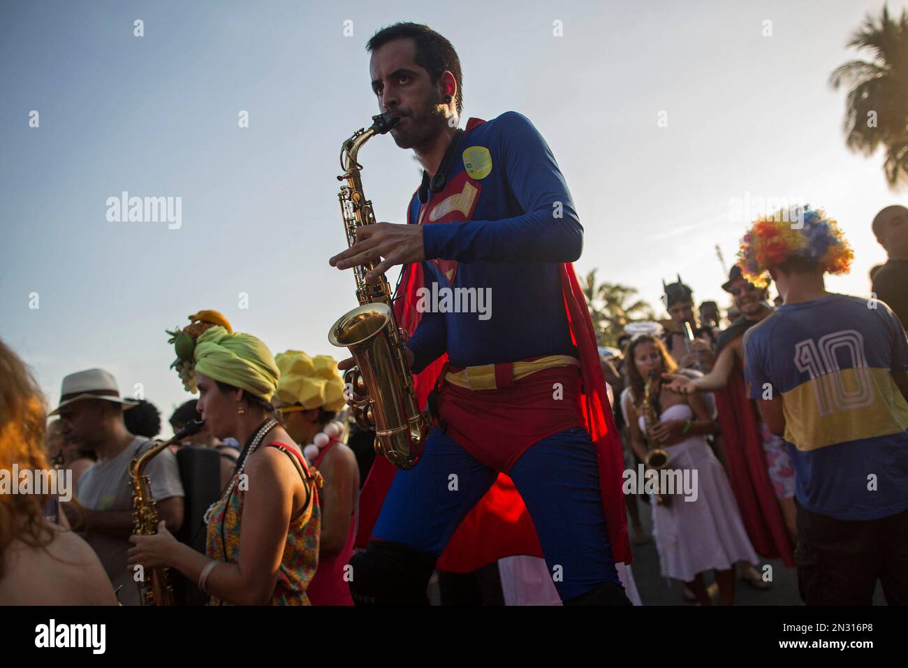 A reveler dressed in a Superman costume, plays a saxophone during the ...