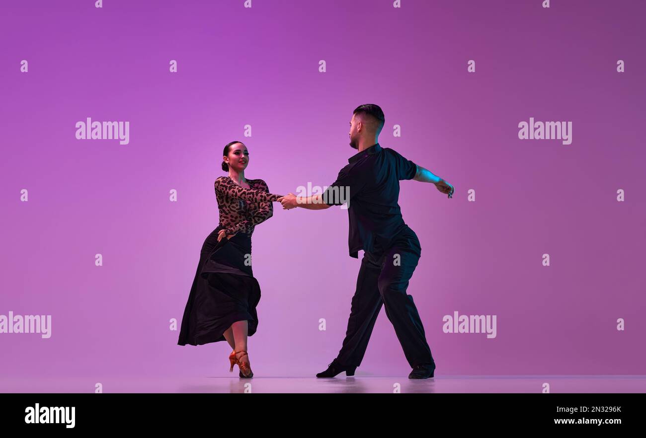 Man and woman, professional dancers in stylish stage costumes performing tango over purple ...