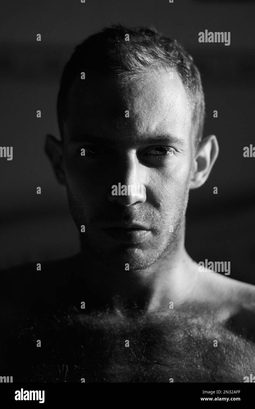 Portrait of handsome man in hard side light facing camera. Half of ...