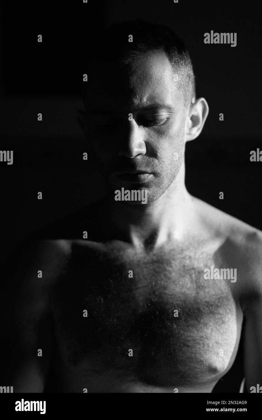 Portrait of handsome man in hard side light meditating. Half of male ...