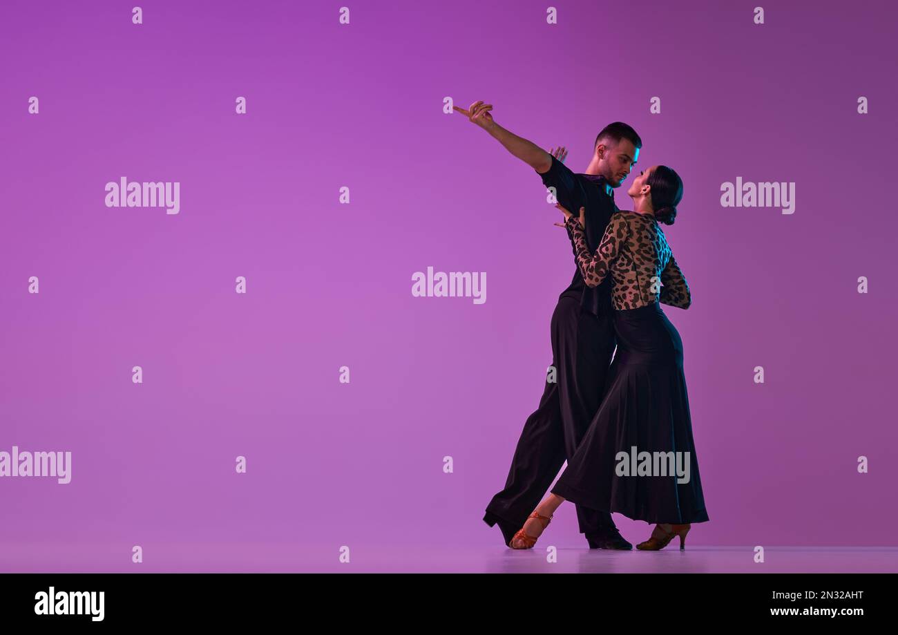 Love. Man and woman, professional dancers in stylish stage costumes performing tango over purple ...