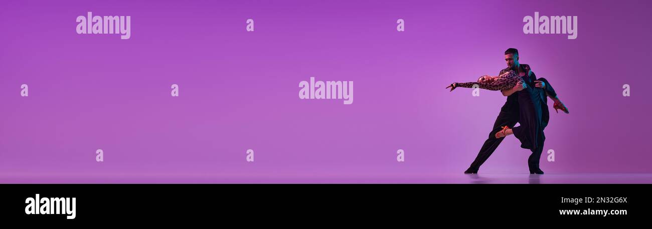 Man and woman, professional dancers in stylish stage costumes performing tango over purple ...