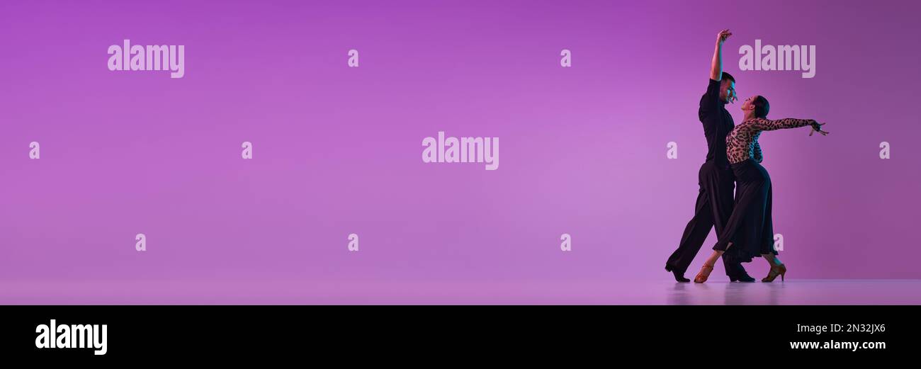 Man and woman, professional dancers in stylish stage costumes performing tango over purple ...