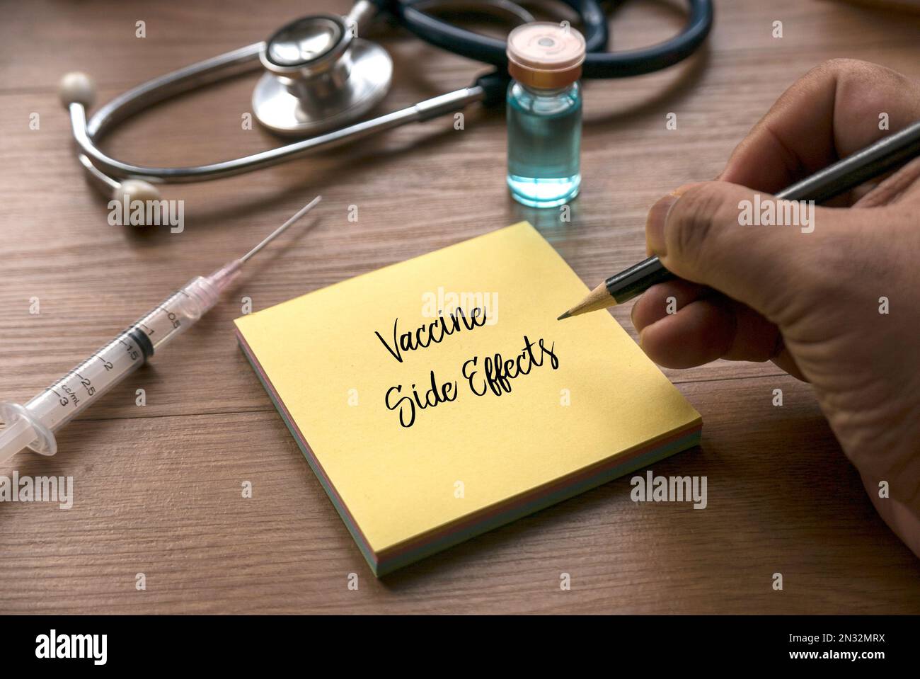 A bottle of vaccine, syringe, stethoscope and a hand writing on yellow ...