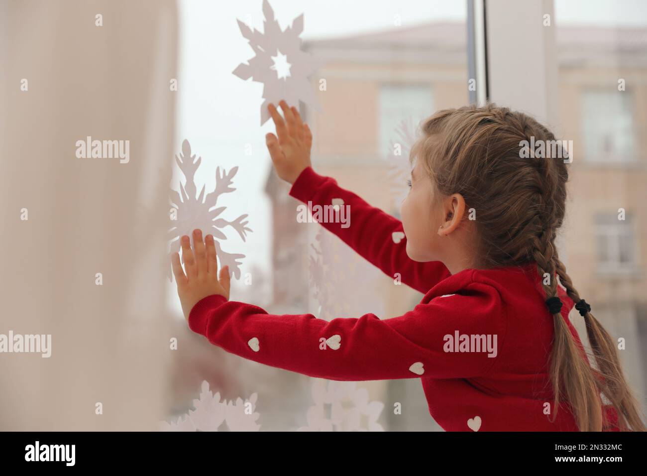 Cute little girl decorating window with paper snowflake indoors Stock ...