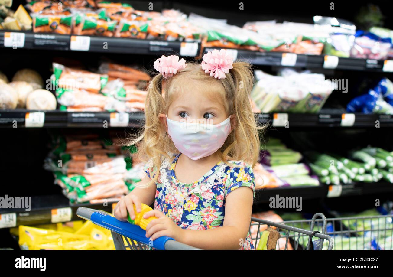 Blonde toddler girl grocery shopping in a face mask. Child in a mask ...