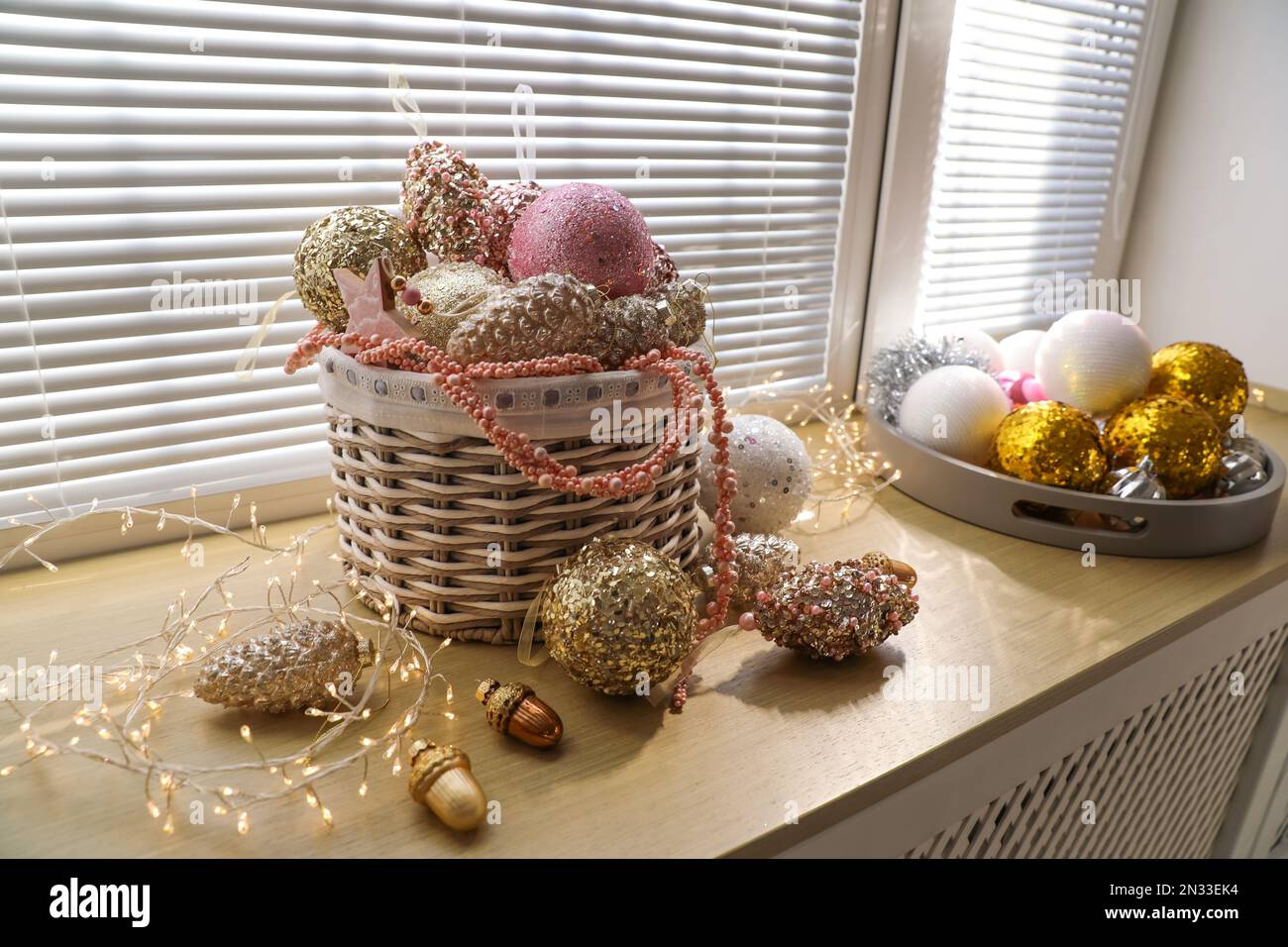 Basket with beautiful Christmas tree baubles and fairy lights on window ...