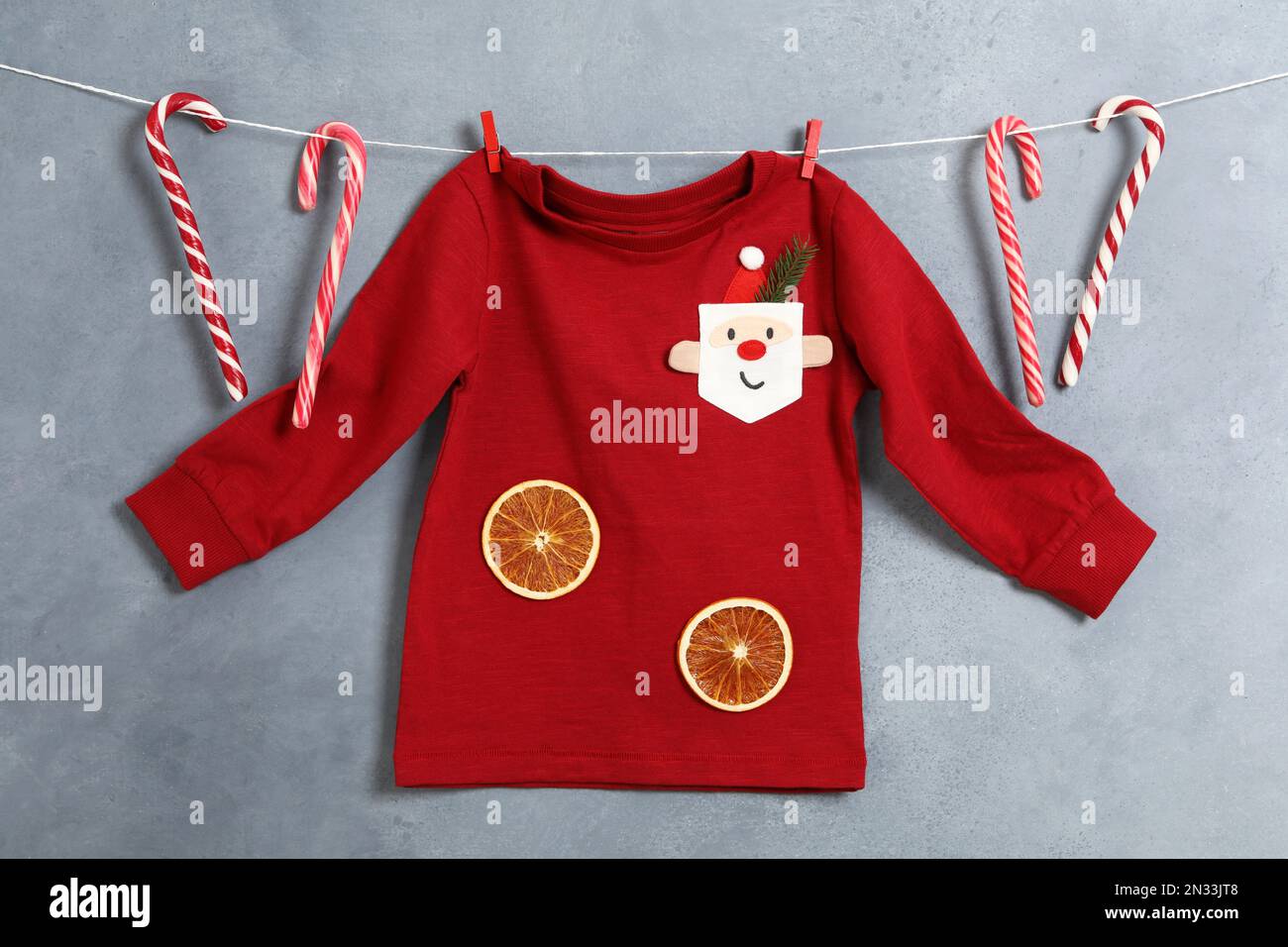 Red jumper and candy canes hanging on grey wall. Christmas baby clothes ...