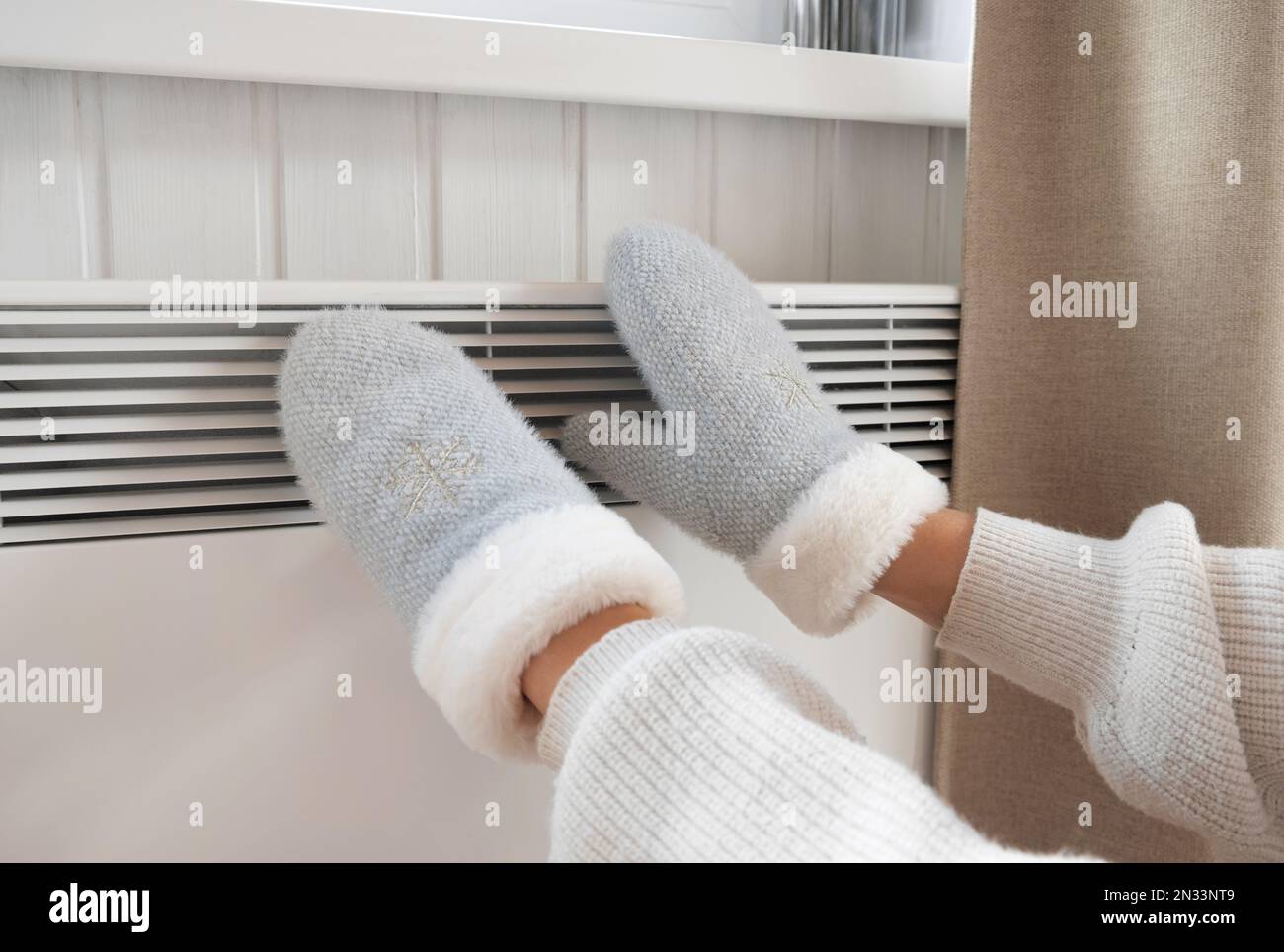 Hands in winter gloves warming up over electric heater. Frozen woman ...