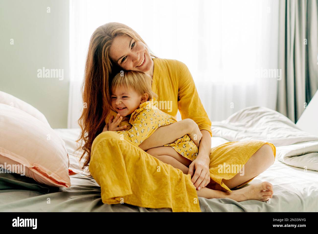 Laughing mother hugging her little daughter while sitting on the bed Stock Photo - Alamy