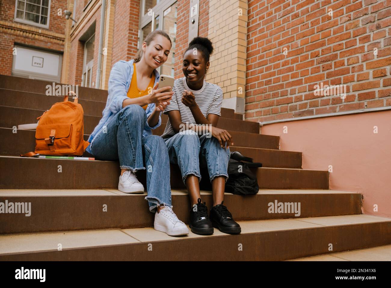 Young multinational girls talking and using cellphone together while ...