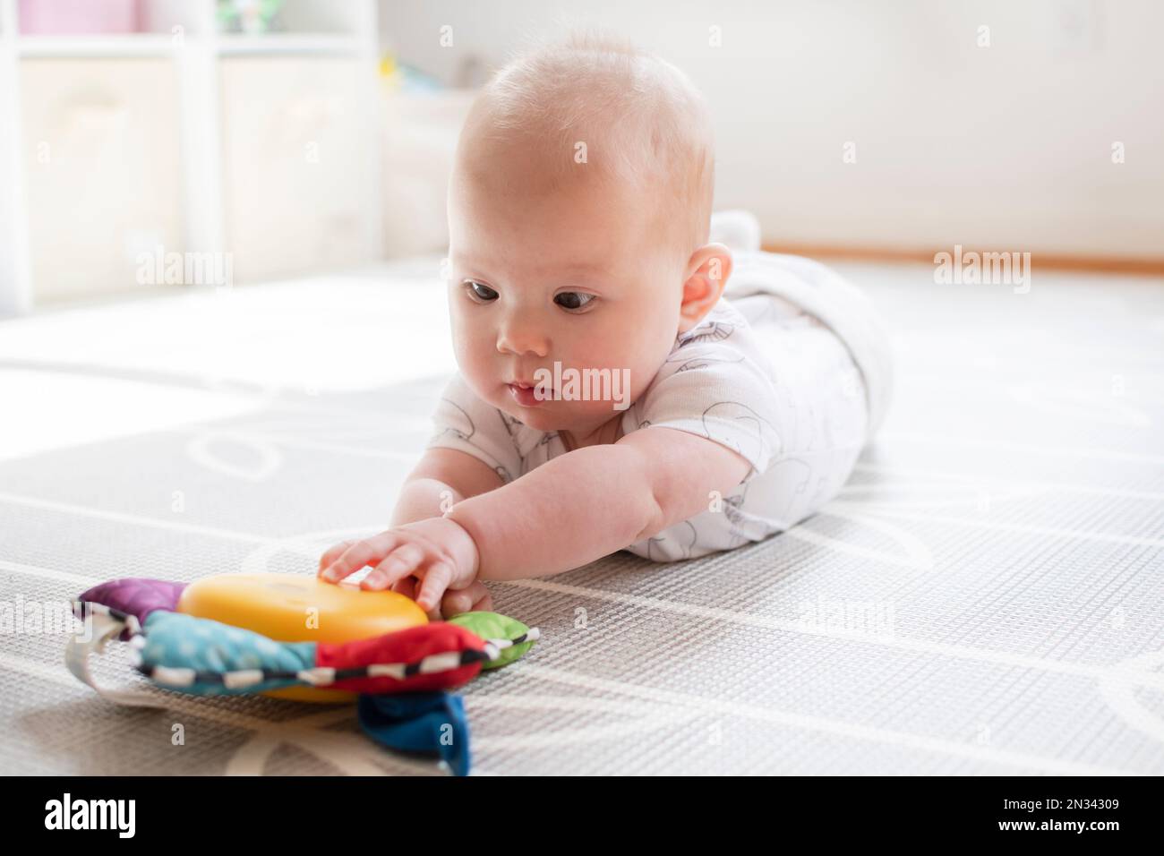 Little baby girl is playing with a toy during tummy time. Baby reaching ...