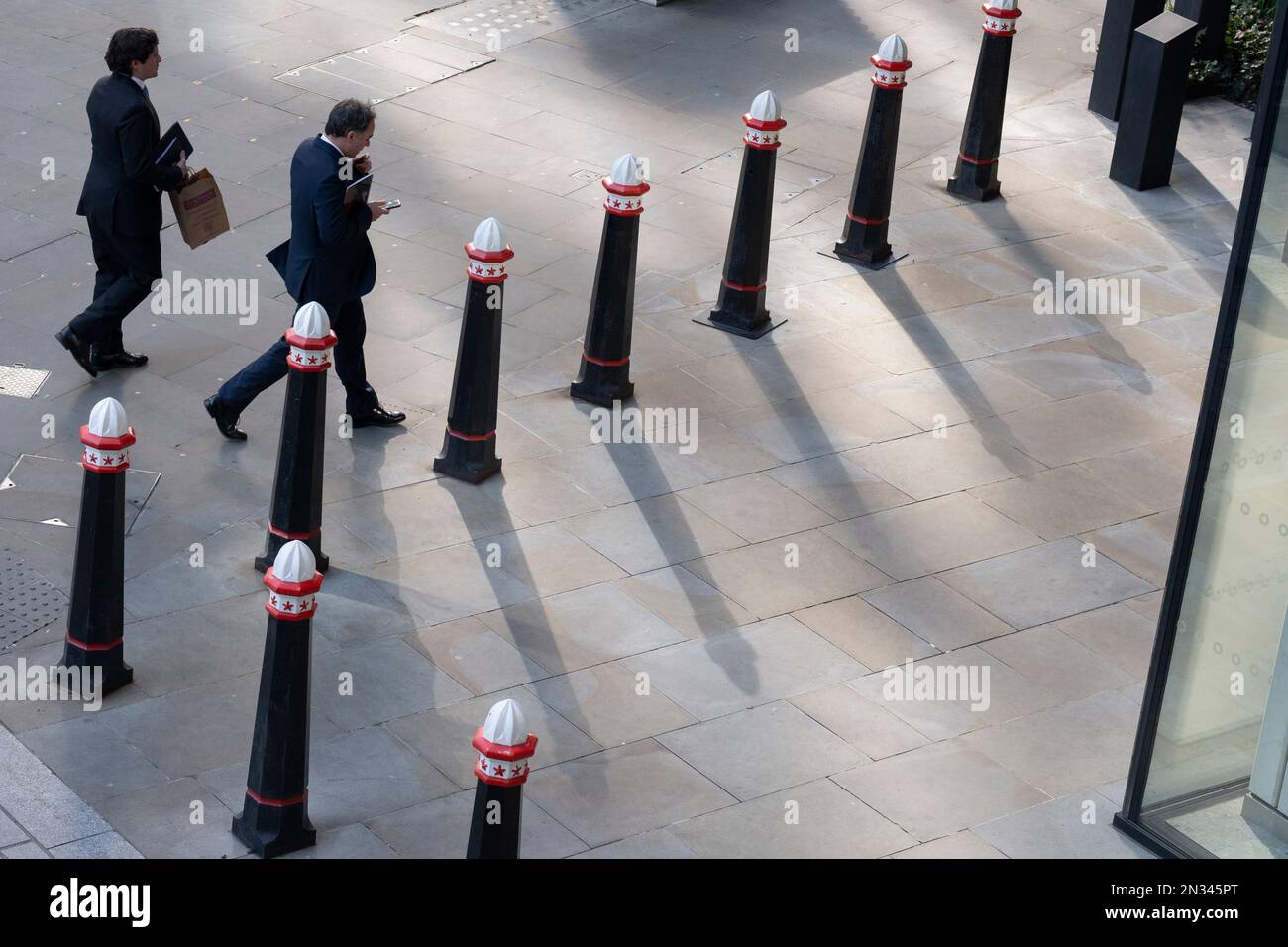 Two businessmen walk through Corporation of London bollards and into an ...