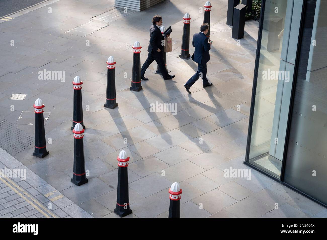 Two businessmen walk through Corporation of London bollards and into an ...