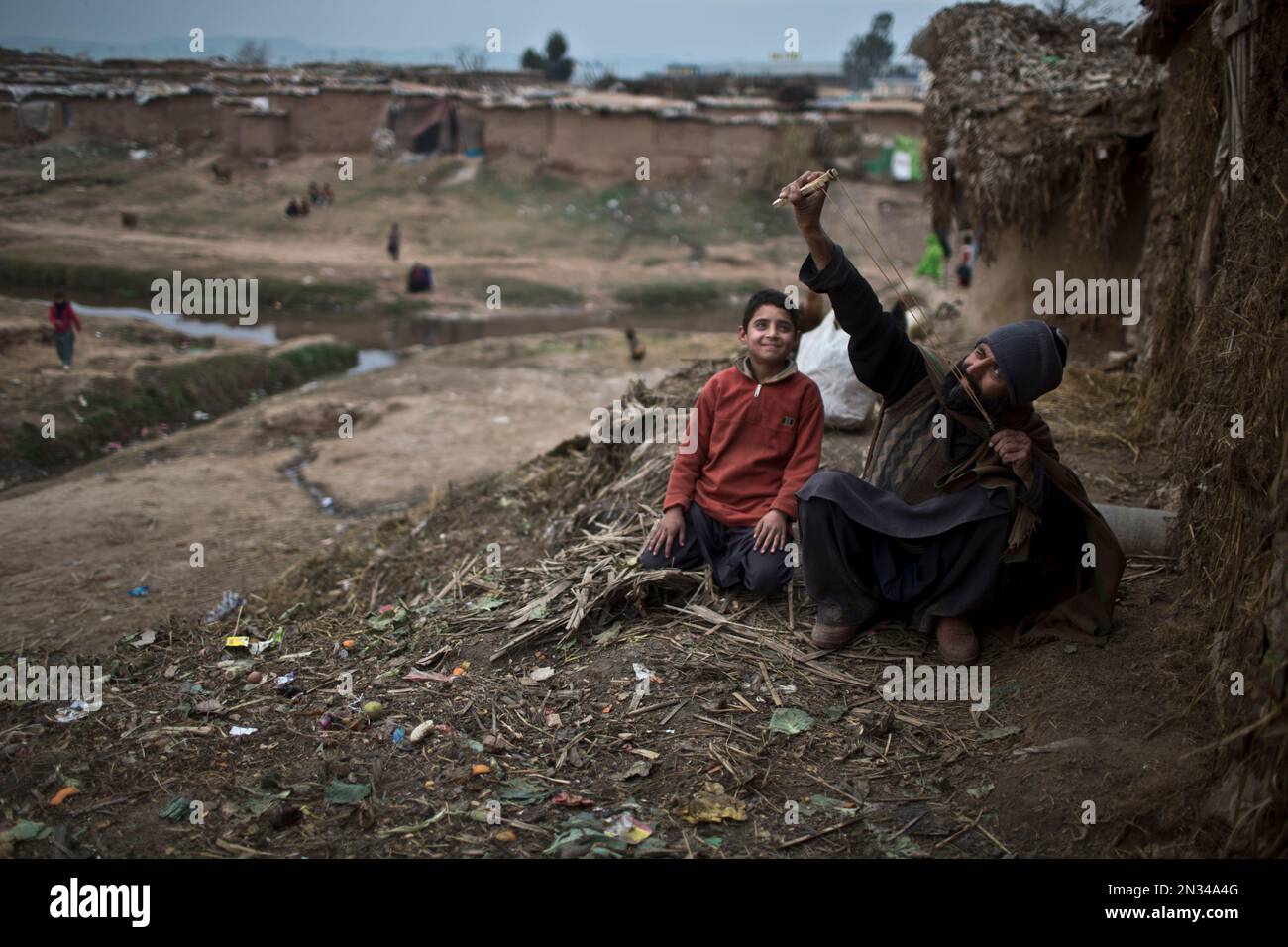 An Afghan refugee man refugee man shows his son how to use a slingshot ...