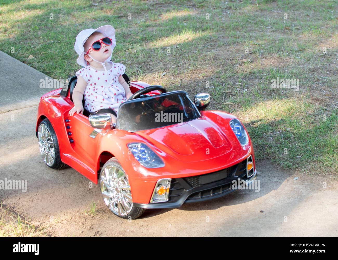 Caucasian baby in white hat riding in an electric convertible red sport ...