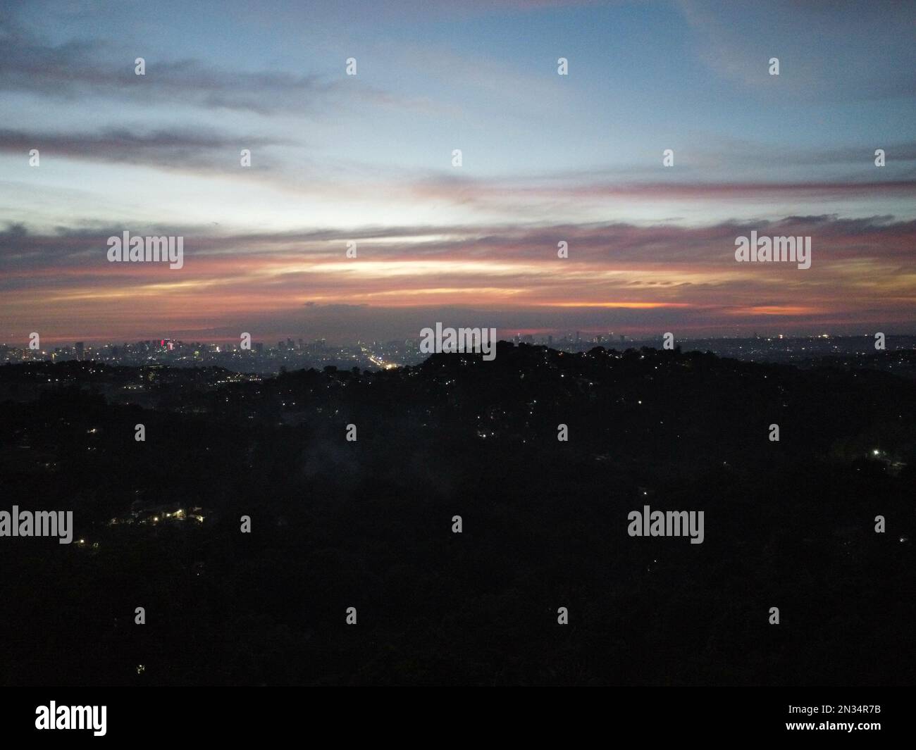 An aerial view of the illuminated cityscape under the shaded sunset sky ...