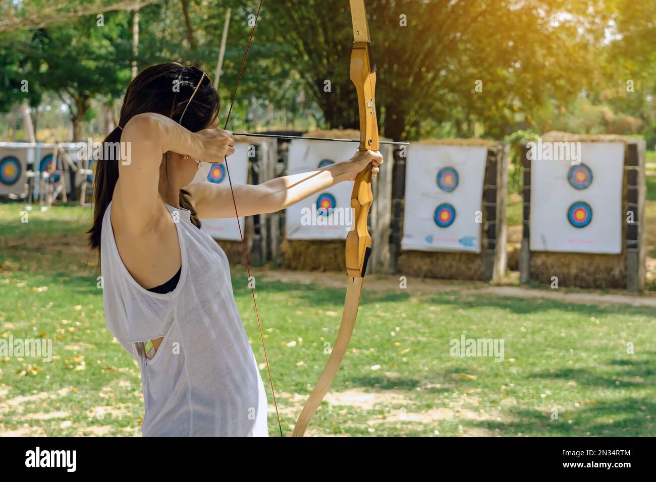 Back view of woman aims archery bow and arrow to colorful target in ...