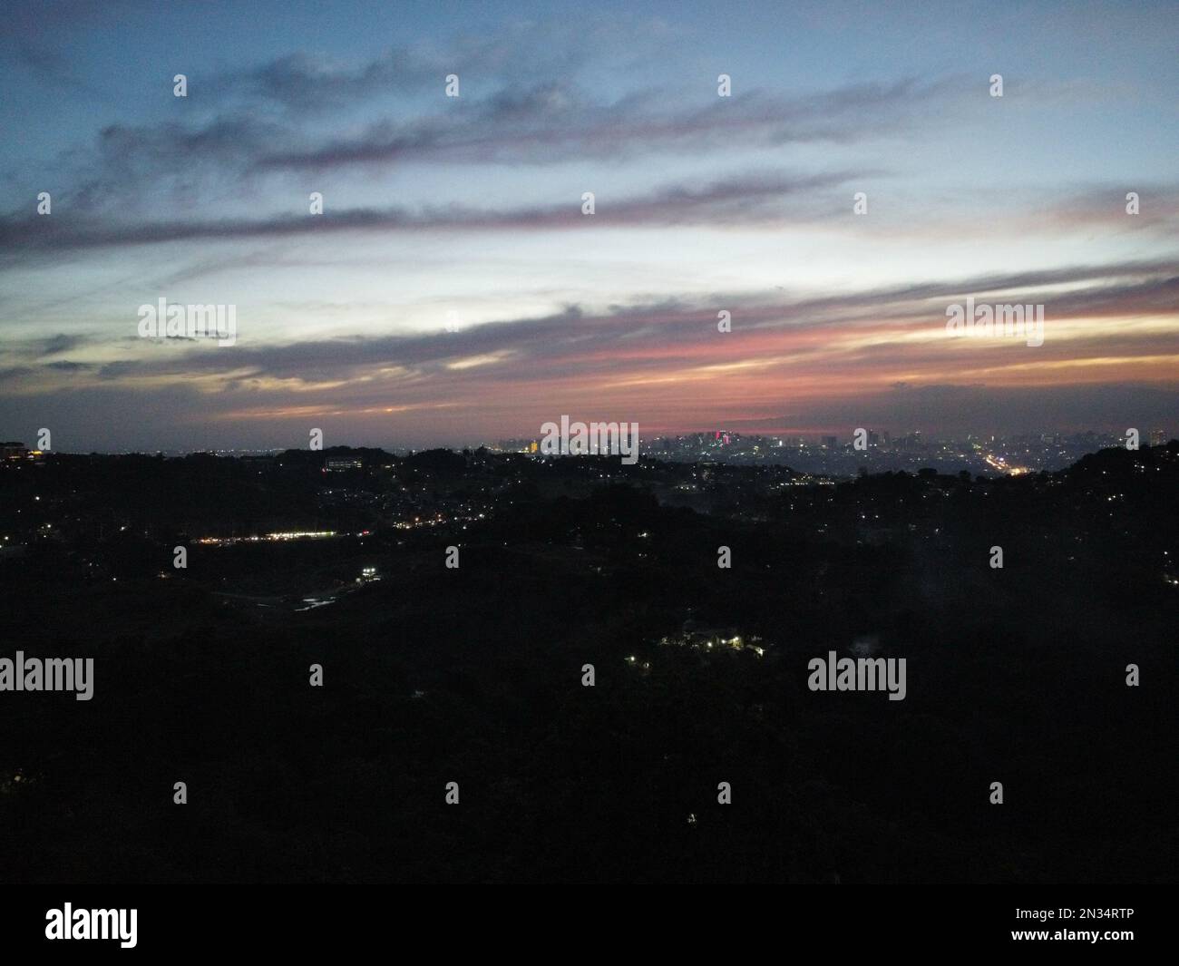 An aerial view of the illuminated cityscape under the shaded sunset sky ...