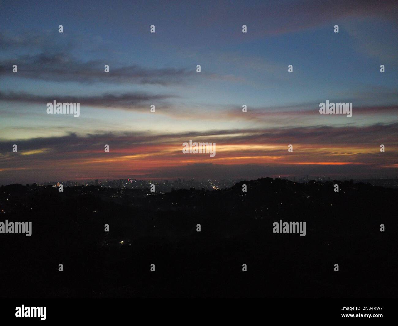 An aerial view of the illuminated cityscape under the shaded sunset sky ...
