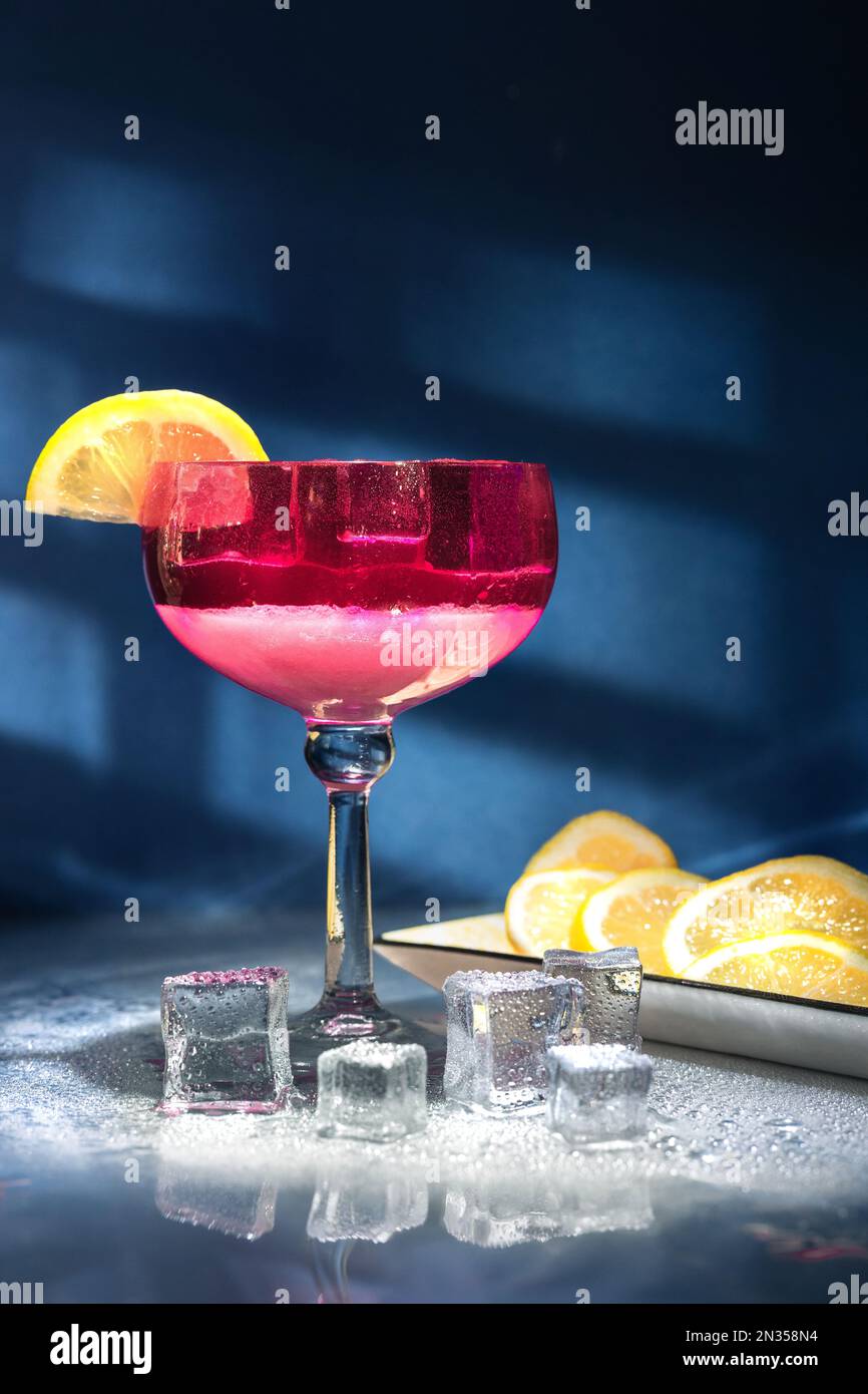 A magenta cocktail with a nice glass, fresh slices of lemon, ice, blue ...