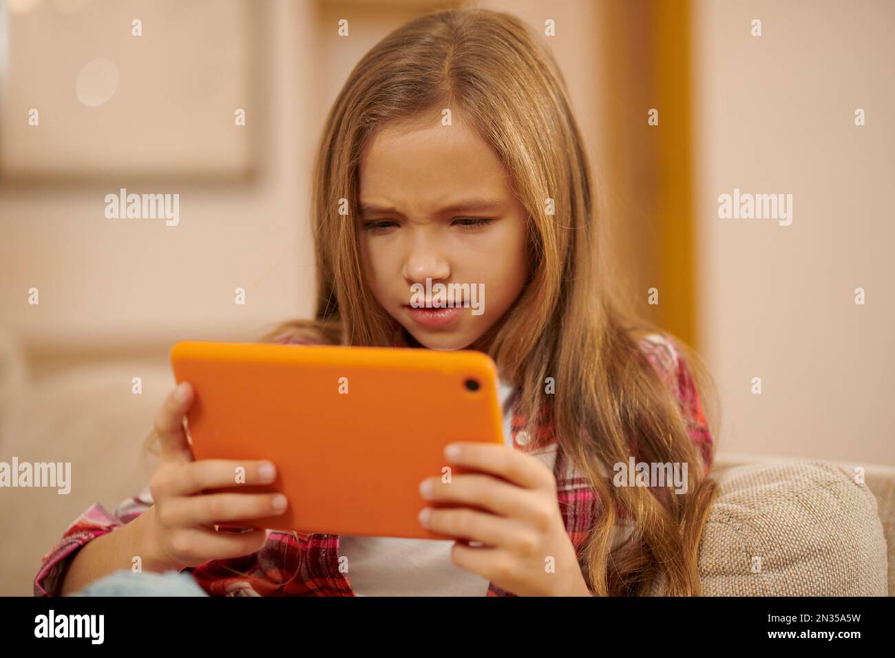 Cute blonde girl with a device in hands looking involved while watching ...