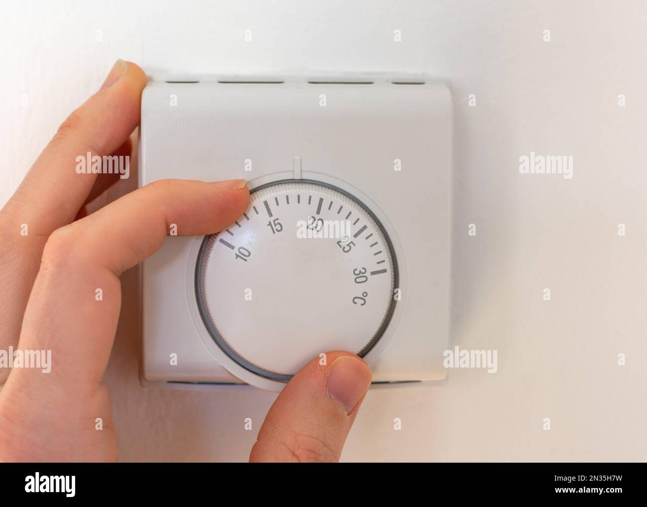 A man turning the thermostat dial, heating and cost of energy concept ...