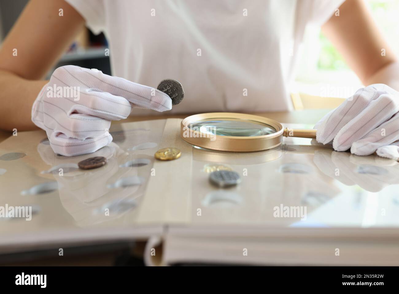 Numismatist in white gloves examines ancient coins collection at table ...