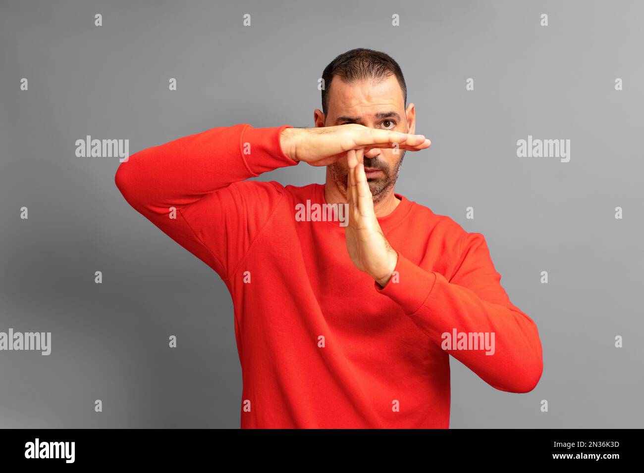 Studio shot of serious man in red jumper making time out gesture need ...