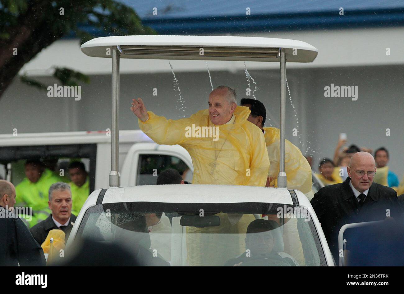 Wearing a yellow raincoat, Pope Francis waves to the faithful as he ...